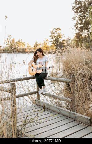 Calm lady looking at the guitar while playing it at the sports ground ...