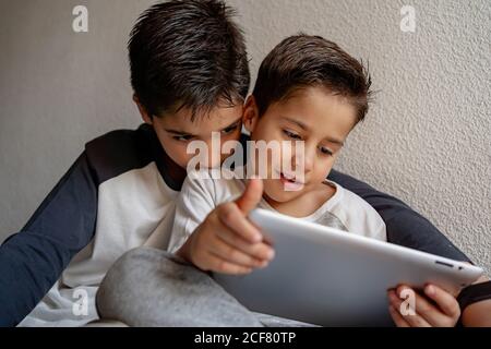 Smiling brothers in sleepwear sitting on cozy bed and watching movie ...