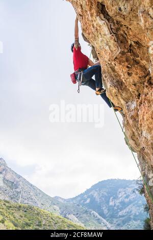 Sportive male alpinist climbing on sheer cliff in summer day Stock ...