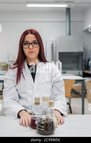 In a laboratory, a woman in a red lab coat observes a large wooden ...