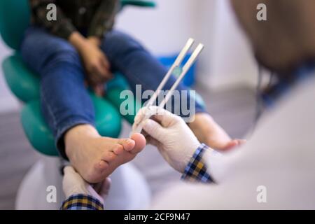 Crop male podiatry doctor in protective gloves cleaning foot of female ...