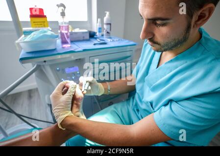 Crop male podiatry doctor in protective gloves cleaning foot of female ...