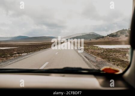 Asphalt road going through plains and hills in front of vehicle on gray ...