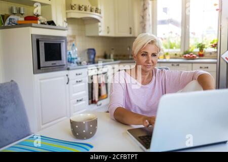 Beautiful mature woman working in a greenhouse, looking at camera and ...