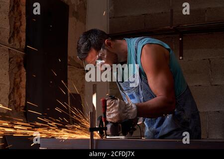 Mechanic in protective gloves cutting metal with red handheld grinder ...