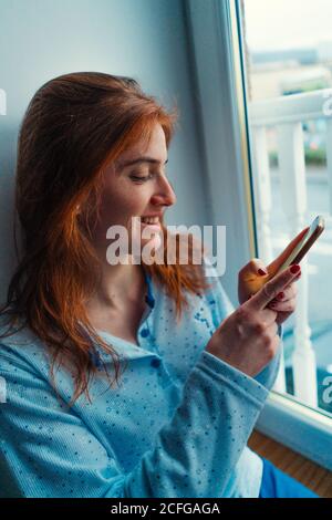Redhead woman using smartphone at home screaming proud and celebrating ...