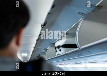 A plane passenger storing hand luggage in the overhead locker on a ...