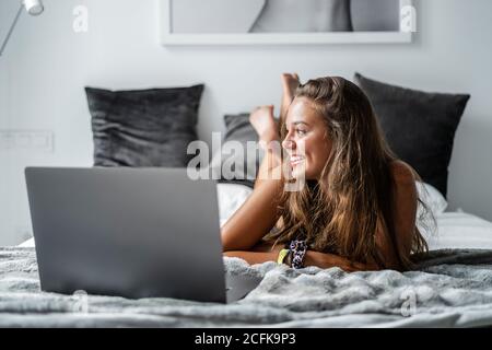 Delighted female in nightwear lying on bed in dark room and watching ...