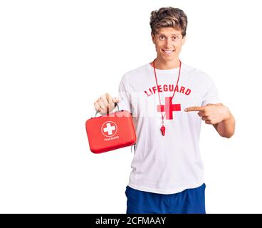 Handsome lifeguard man wearing t-shirt with red cross and whistle over ...