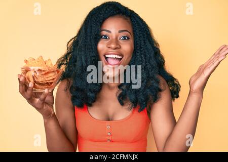 Beautiful african woman holding nachos potato chips smiling happy and ...