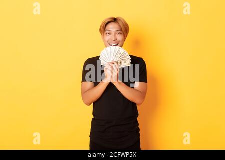 Cheerful winning handsome asian guy, smiling pleased and holding money ...