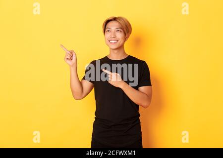 Portrait of handsome korean blond guy, pointing fingers upper left ...