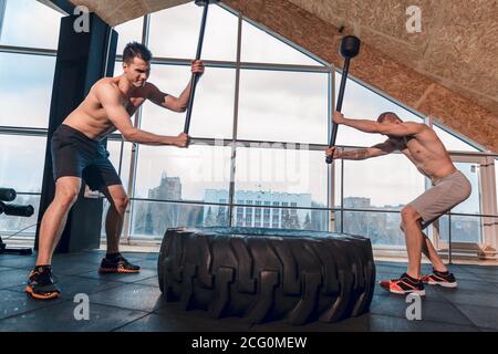 two Male fitness models training workout witth heavy and big tire and ...