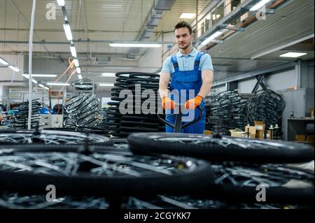 Male worker carries bicycle wheels on a cart on factory. Bike rims ...