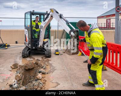 Workmen using Bob Cat backhoe excavator excavating a cable trench to ...