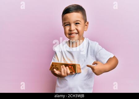 Adorable latin toddler holding gold ingot pointing thumb up to the side ...
