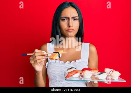 Young brunette woman eating omelet sushi using chopsticks afraid and ...