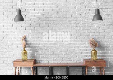 Wooden stand with decor and lamps near grey brick wall in room Stock ...