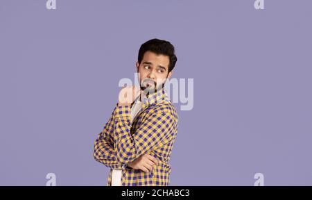 Thoughtful Indian guy looking over his shoulder at empty space, lilac ...