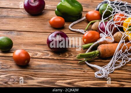 fresh ripe vegetables scattered from string bag on wooden table ...