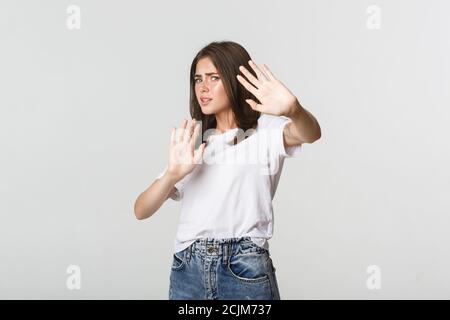 Scared and insecure cute girl raising hands in stop gesture, defending ...