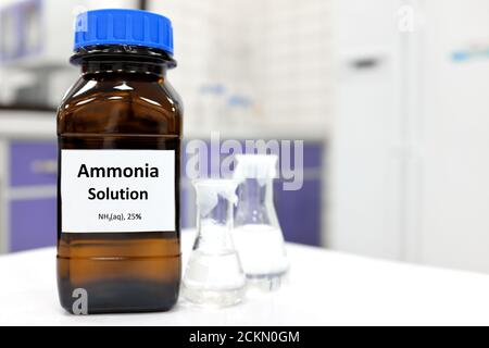 Ammonia solution. Laboratory bottle and beaker of ammonia solution. Ammonia solution is a ...