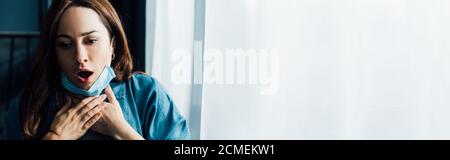 panoramic crop of scared woman with open mouth touching medical mask ...