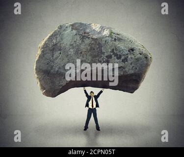 Strong businessman lifting up a huge heavy stone above his head as ...