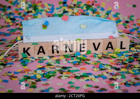 German word KARNIVAL on wooden blocks under a face mask with confetti ...