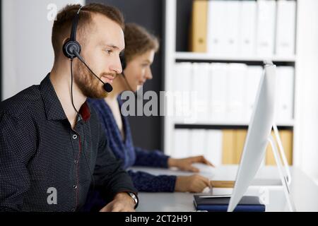 Red-bearded businessman talking by headset near his female colleague ...