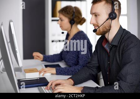 Red-bearded businessman talking by headset near his female colleague ...