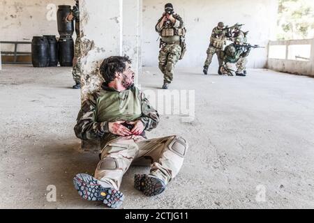 Wounded on stomach soldier, sitting at floor, squeezing bleeding wound ...