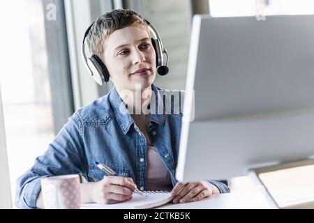 Headset-wearing agent taking notes in notebook at office desk, with ...