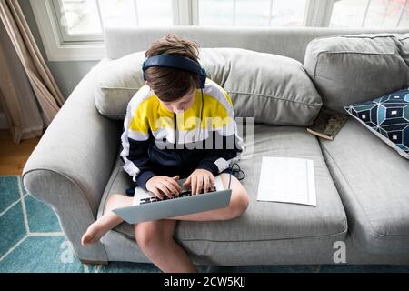 Teen boy using laptop with headphones while sitting isolated on white ...