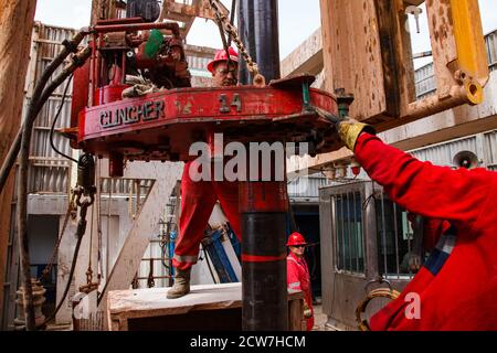 Workers with electric clincher tool on drilling rig. Red work wear ...