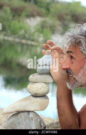Mature man doing stone piles along the river Stock Photo - Alamy