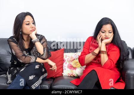 Two angry friends after a quarrel sitting on a couch and looking at the ...
