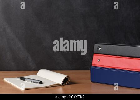 Three different binders laying on a teachers desk in front of a chalk ...