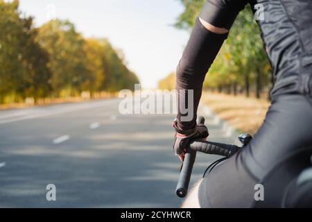Hands of a cyclist resting on road bike handlebars, road view with copy ...