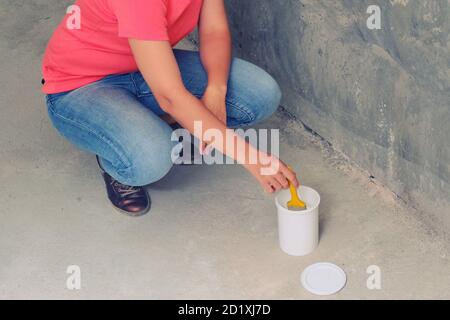A woman squats and dips a brush into a can of paint, isolated on a ...