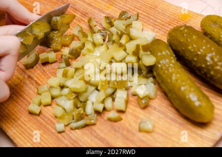 Women's hands cut pickles into cubes on a wooden cutting Board in the ...
