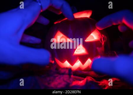 Women's blue hands with painted nails reach for a glowing evil pumpkin ...