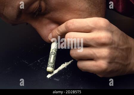 Male hands sniffing drugs through a dollar on a black background close ...