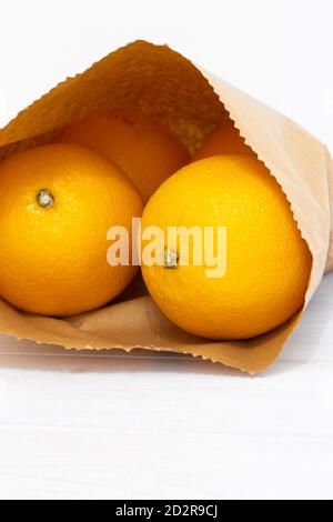 Oranges in a brown paper bag on a white wood background ...