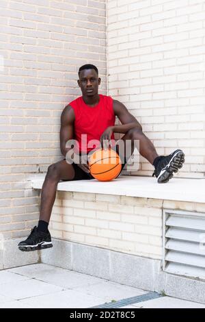 African American male basketball player sitting on sports ground and ...