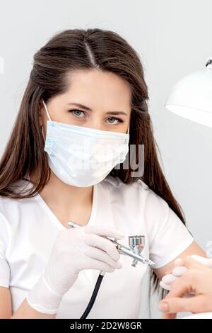 Portrait of manicure master uses airbrush wearing mask in nail salon ...