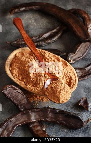 Carob pod and powder in wooden bowl isolated on white background with ...