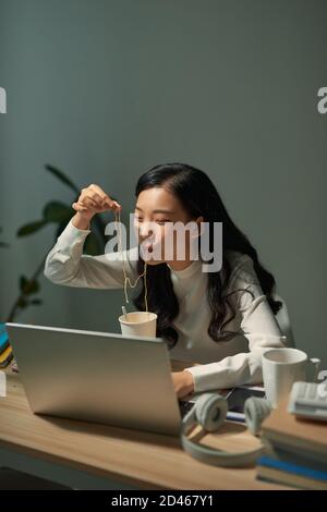 Hungry student eating noodle while learning at home Stock Photo - Alamy