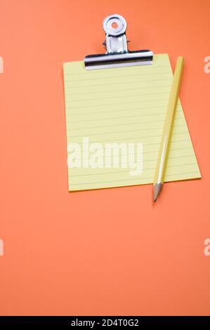 Vertical shot of a notepad and a paper clipper isolated on an orange ...