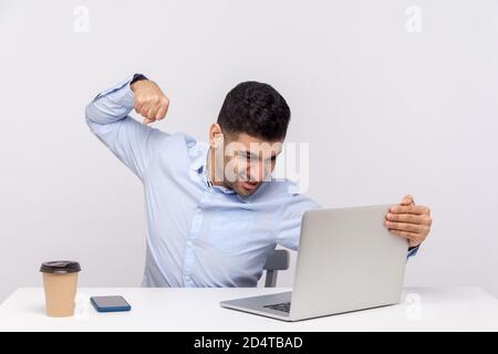 Angry businessman punching laptop screen, looking with mad expression ...